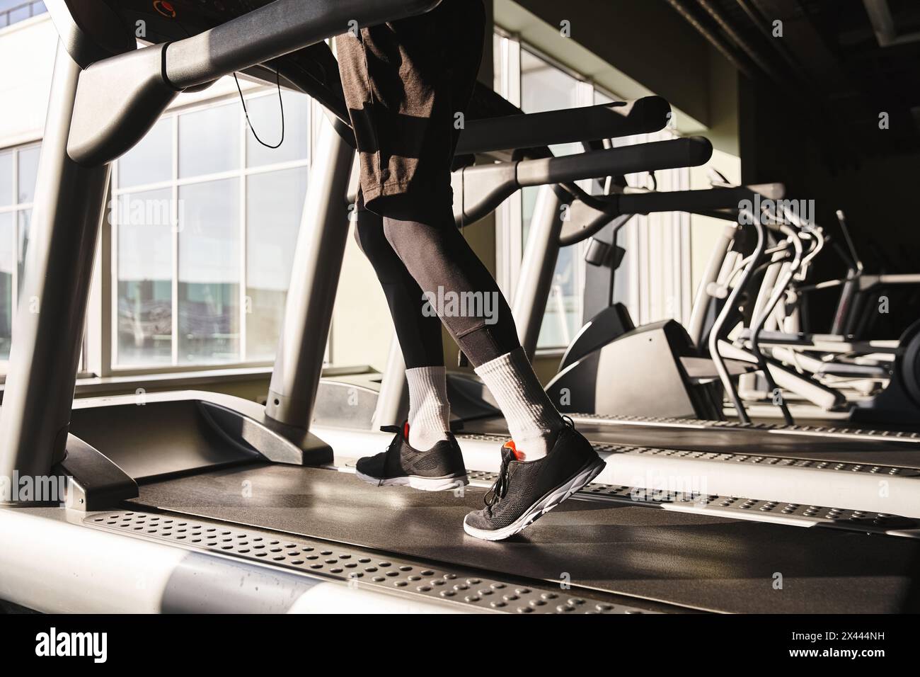 A man in active wear is running on a treadmill in a gym setting, with ...
