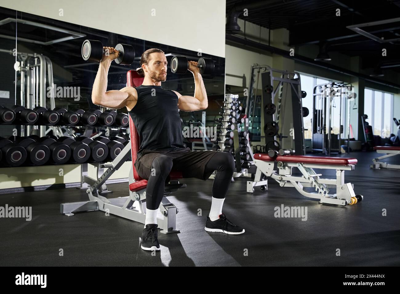 A focused man in active wear is lifting weights on a bench press in a ...