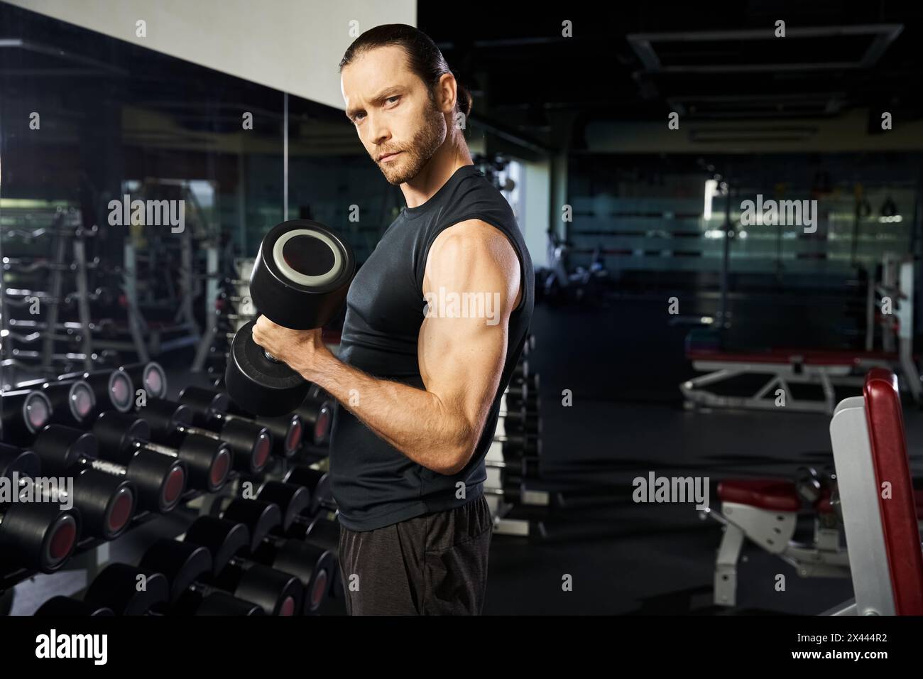 An athletic man in active wear lifts a dumbbell in a gym, showcasing ...