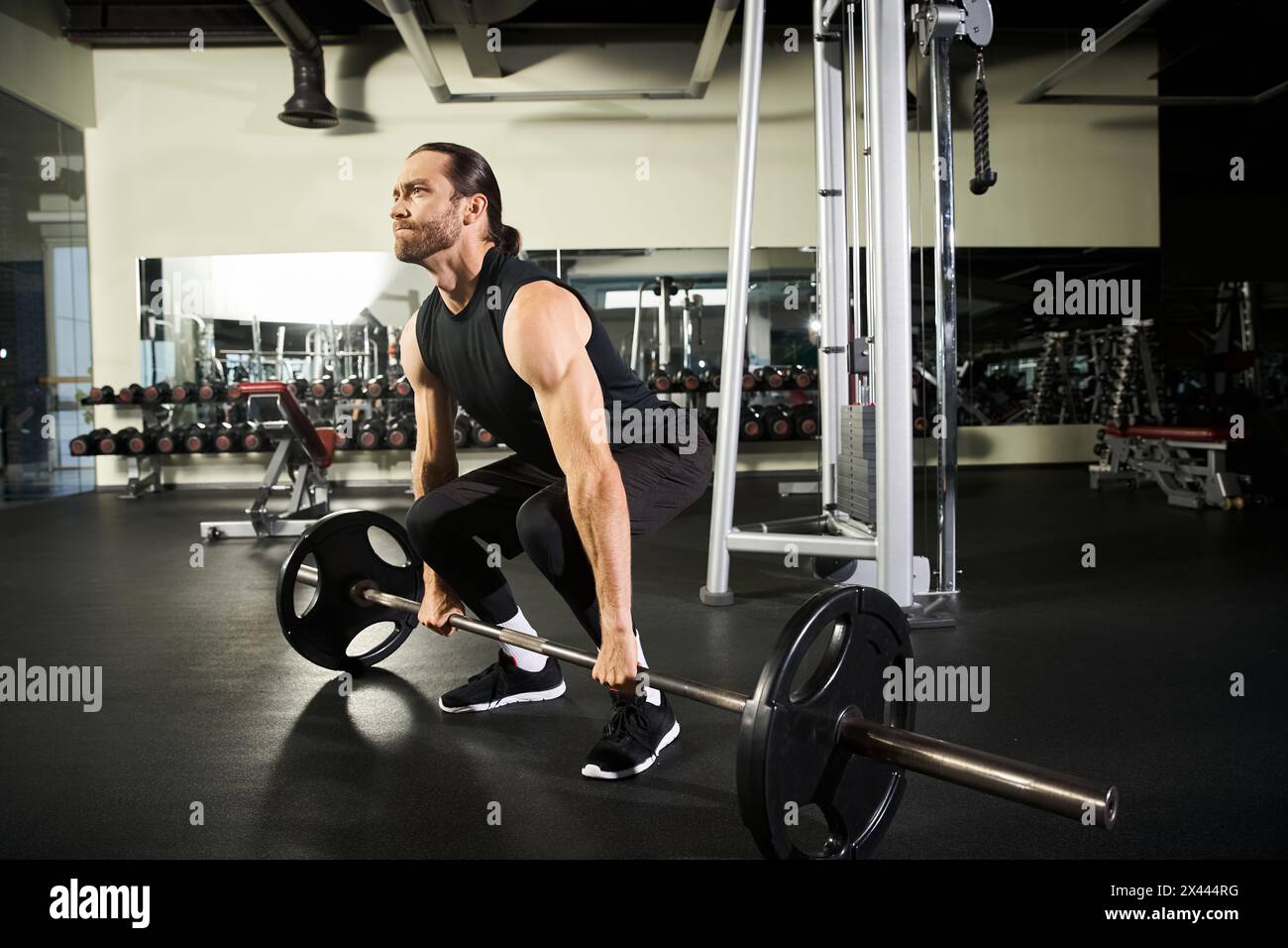 A focused man in active wear performs a squat with a barbell in a gym ...