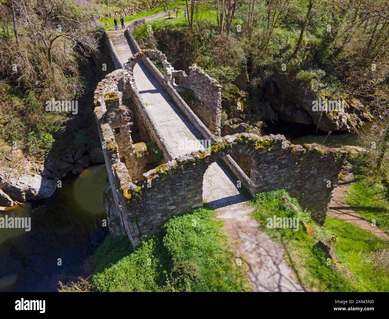 Ruins of a historic bridge with moss-covered stones over a river in a ...