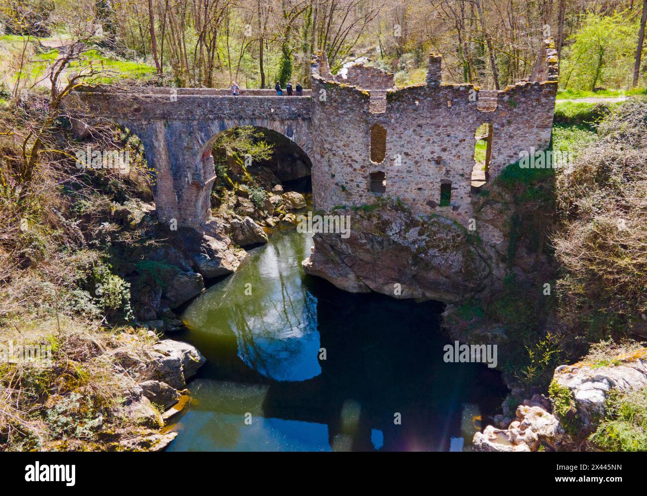 Partially destroyed old stone bridge over a river, surrounded by lush ...