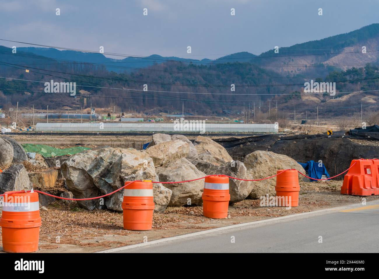 Orange traffic barrels on side of rural road in front of large boulders ...