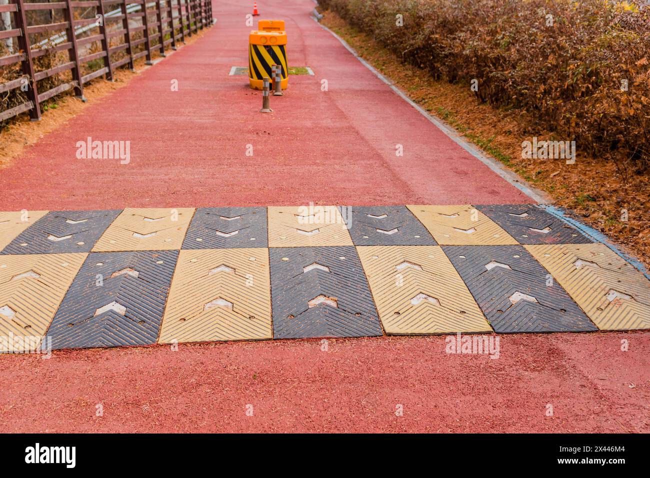 Yellow and black rubber speed bump across red asphalt bicycle path with ...