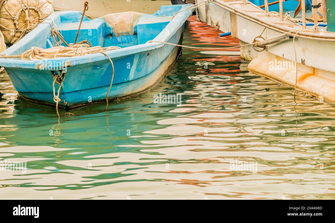 Closeup of small blue fishing boat floating in water tied to a larger ...