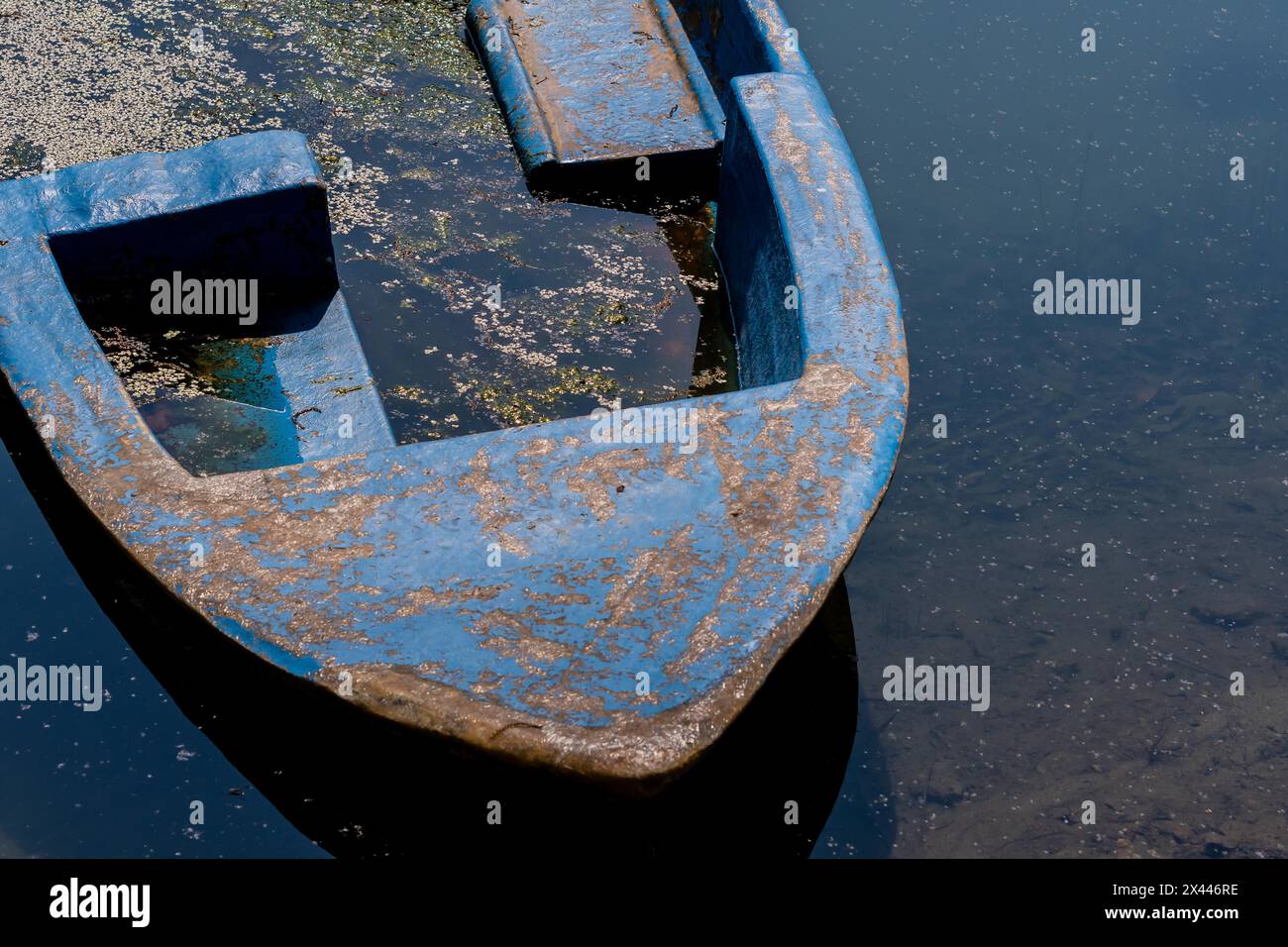 Closeup of blue fishing boat filled with dirty water floating in river ...