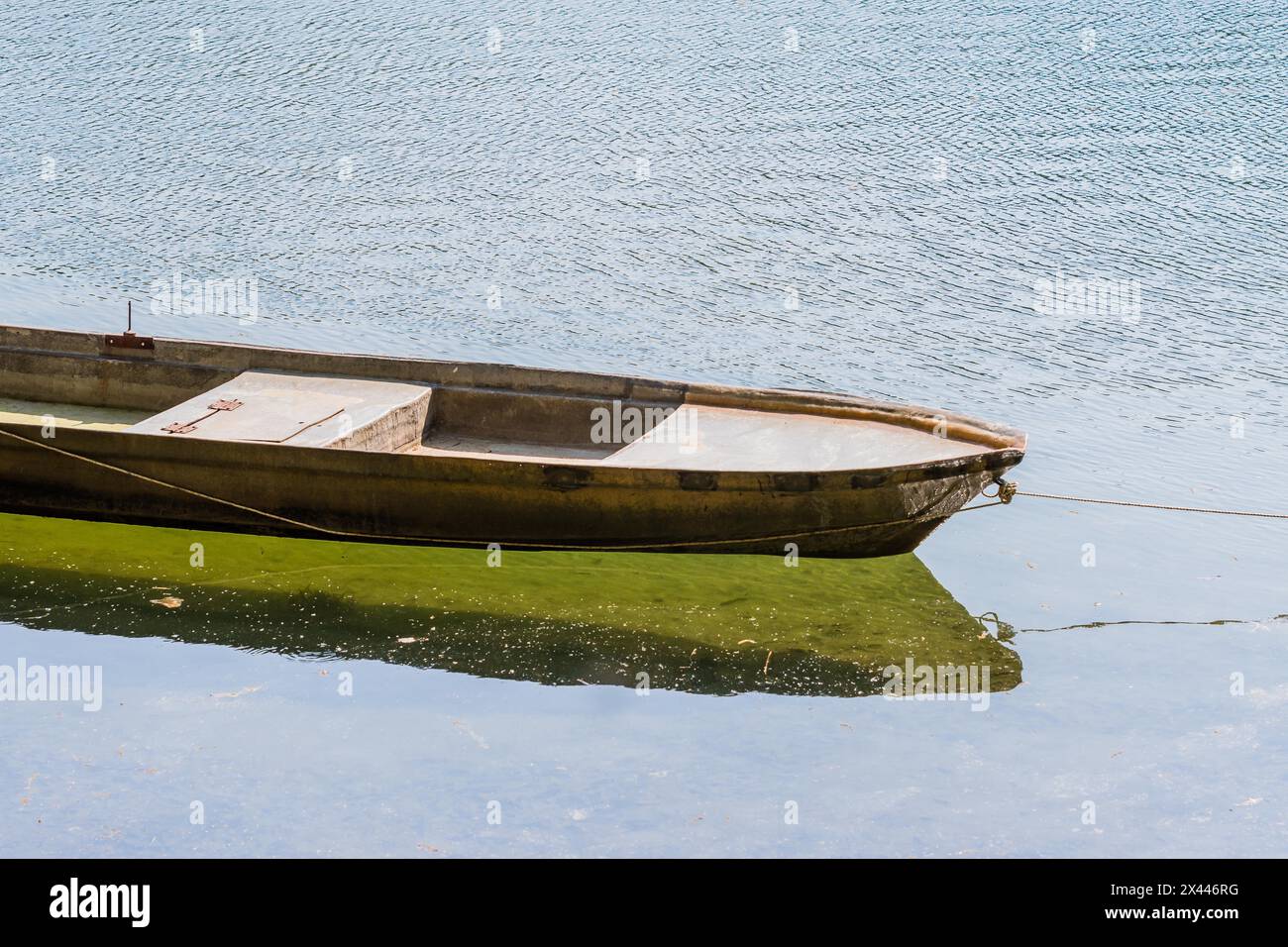 Small metal fishing boat floating in a river with its reflection in the ...