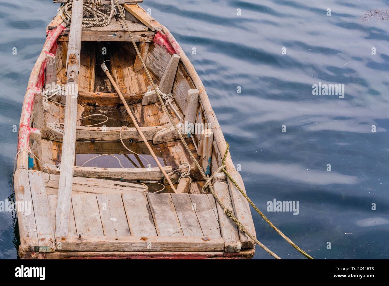 Small wooden rowboat with floating in calm water with ropes leading to ...