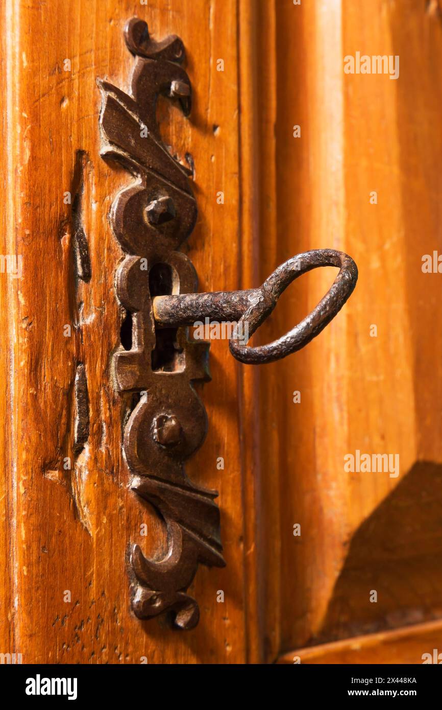 Close-up of antique metal key in keyhole of ornate door lock on wooden ...