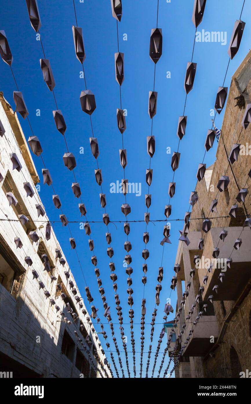 Rows of folded metal boat hats hanging from cables over an alley in the ...
