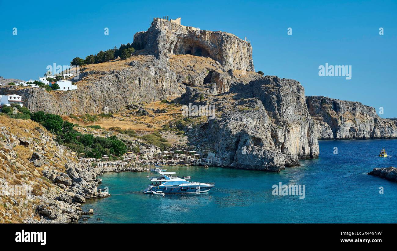 Medieval castle above a town on the coast with boats in the water ...