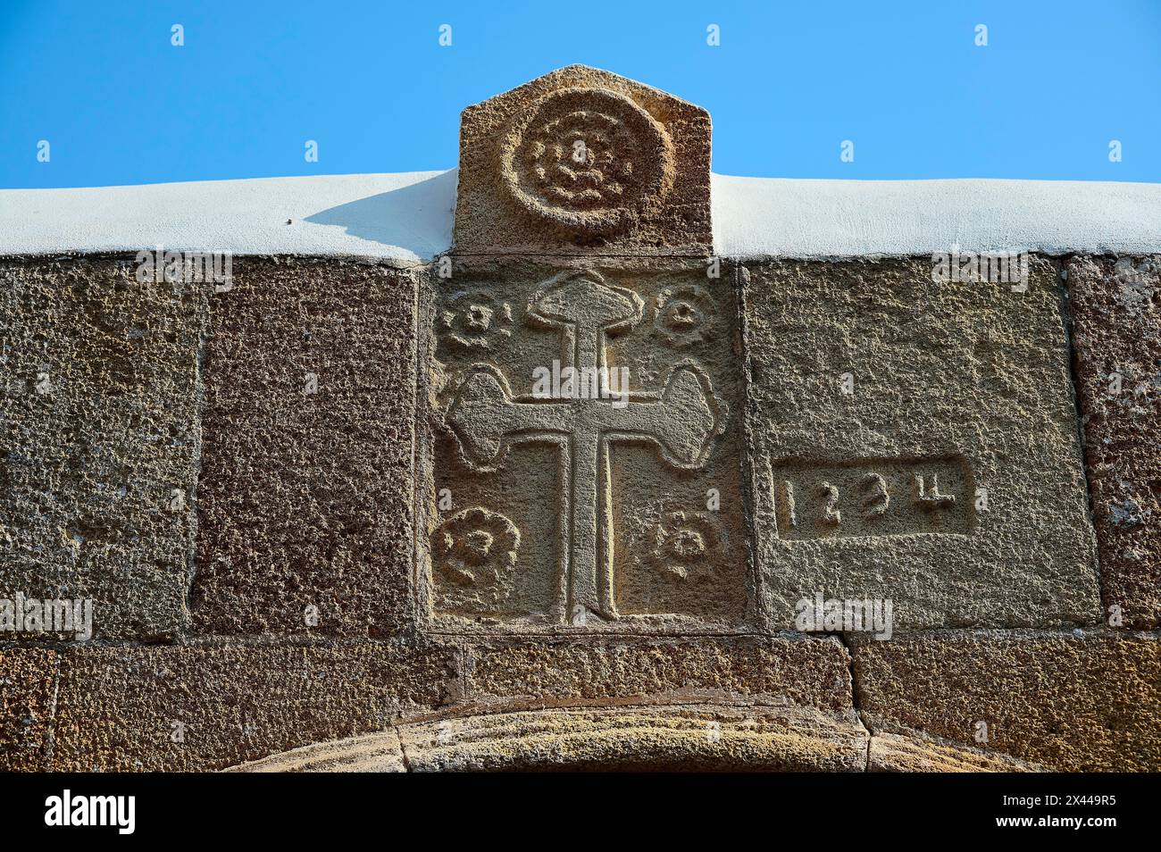 A stone cross with engraved symbols and dates against a clear blue sky ...