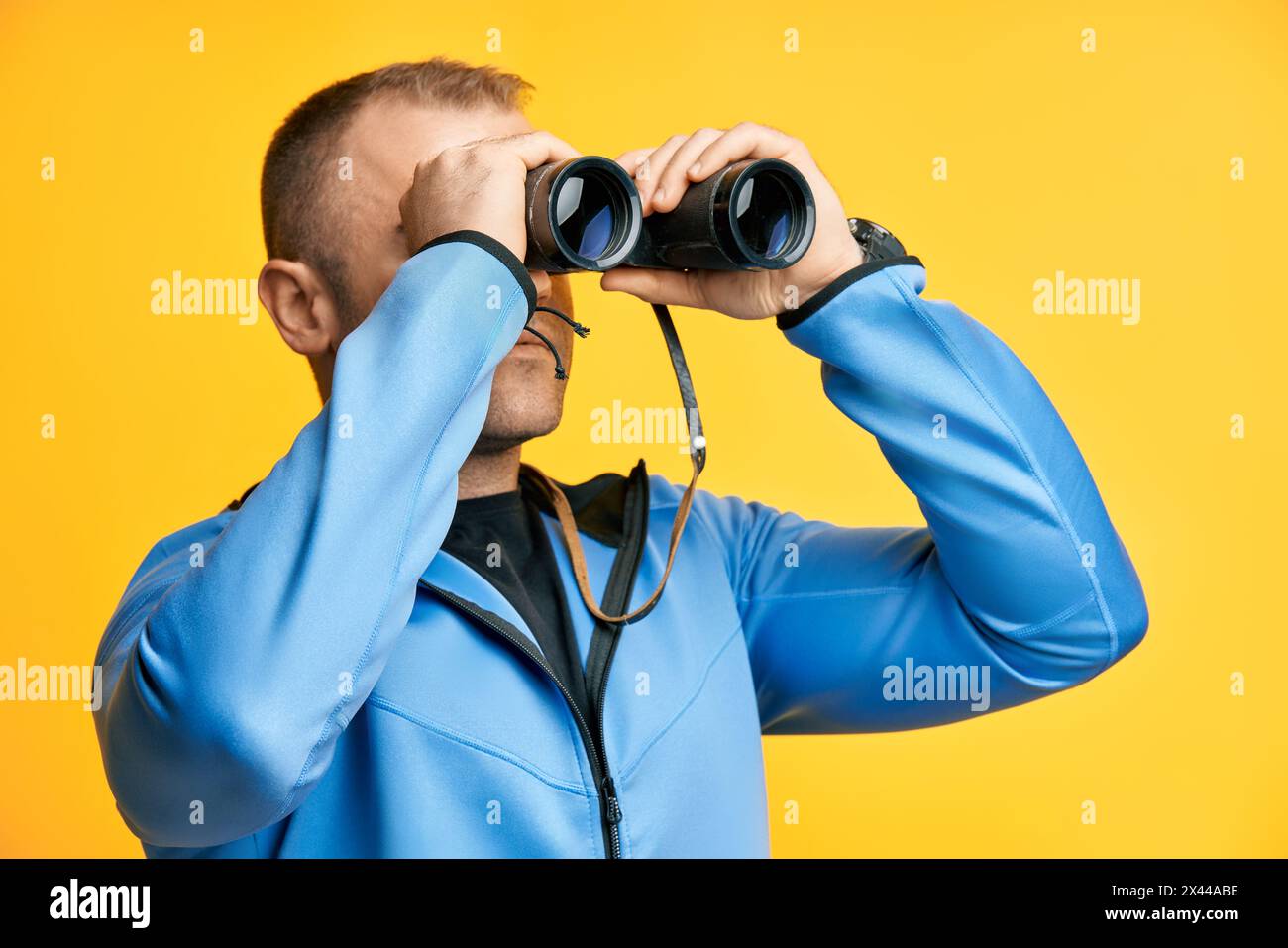 Young man looking through binoculars isolated over yellow background ...