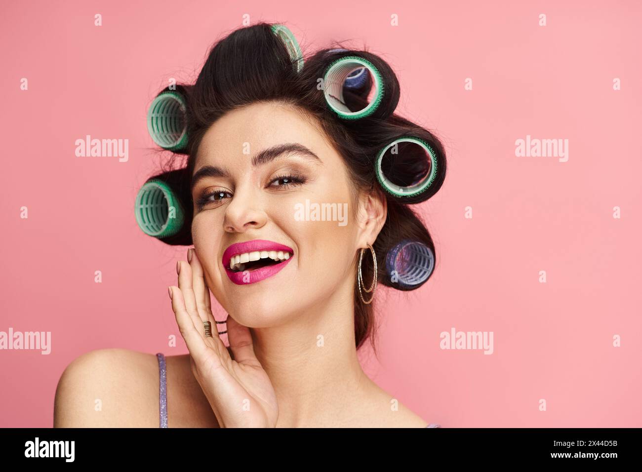 A woman with curlers in her hair striking a pose against a vibrant ...