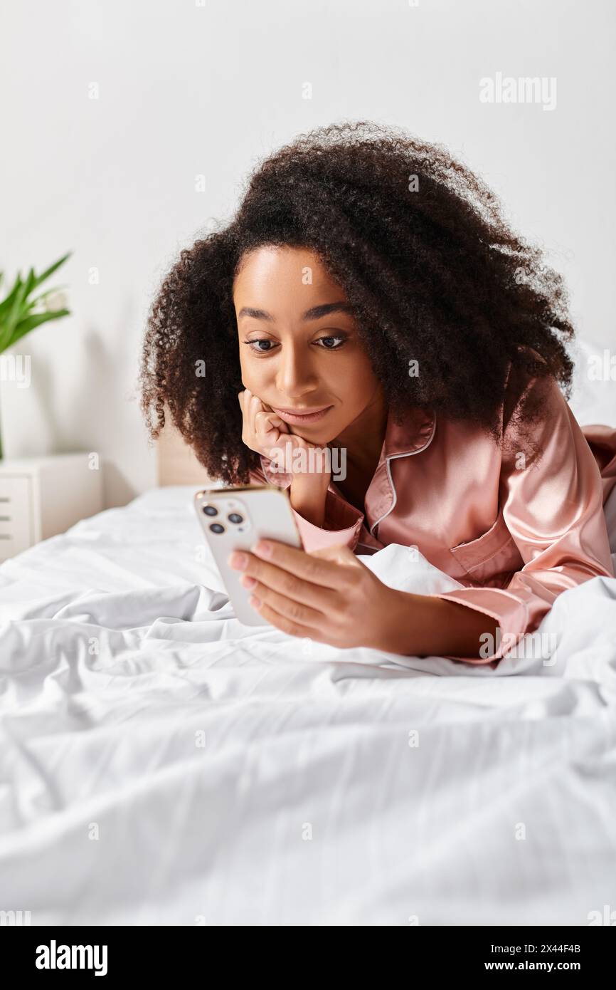 Curly African American woman in pajamas lying on bed, engrossed in ...