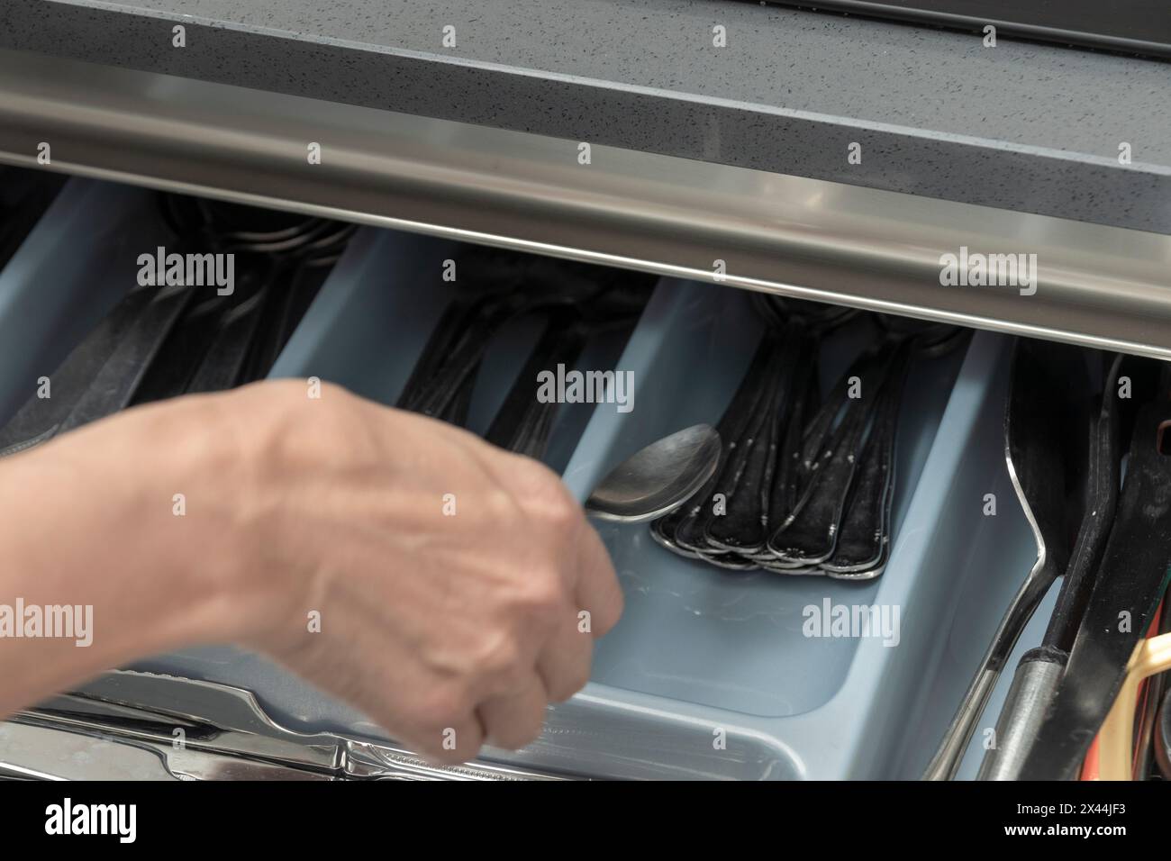 hand reaching into a drawer for utensils, depicting a common household ...