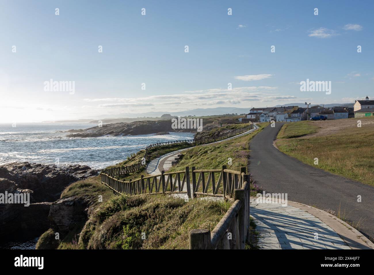 picturesque coastal village with houses, a path, cliffs, and the ocean ...
