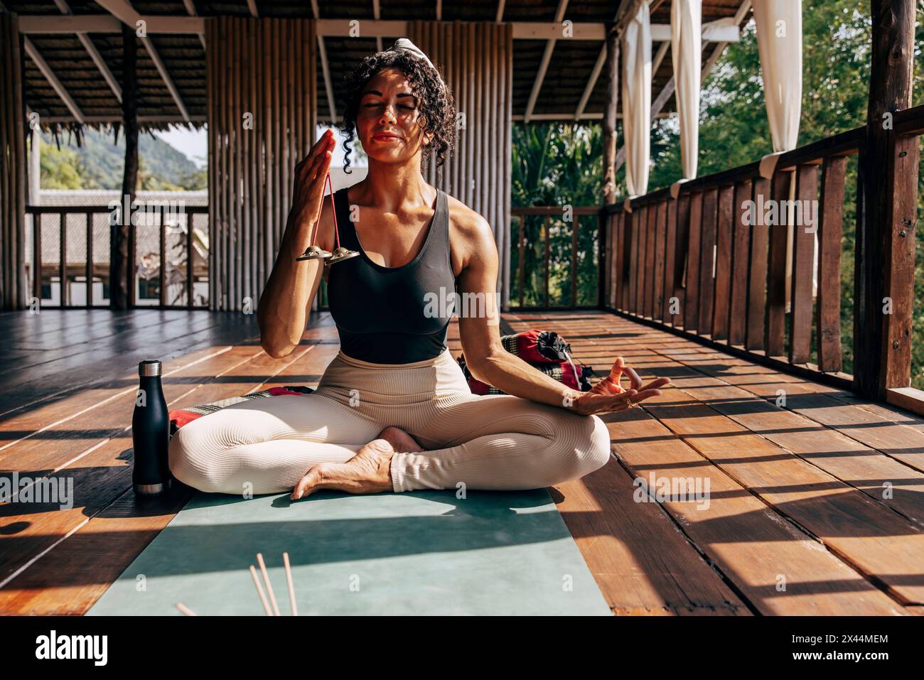 Mature woman holding Tibetan bells and meditating while sitting on yoga ...
