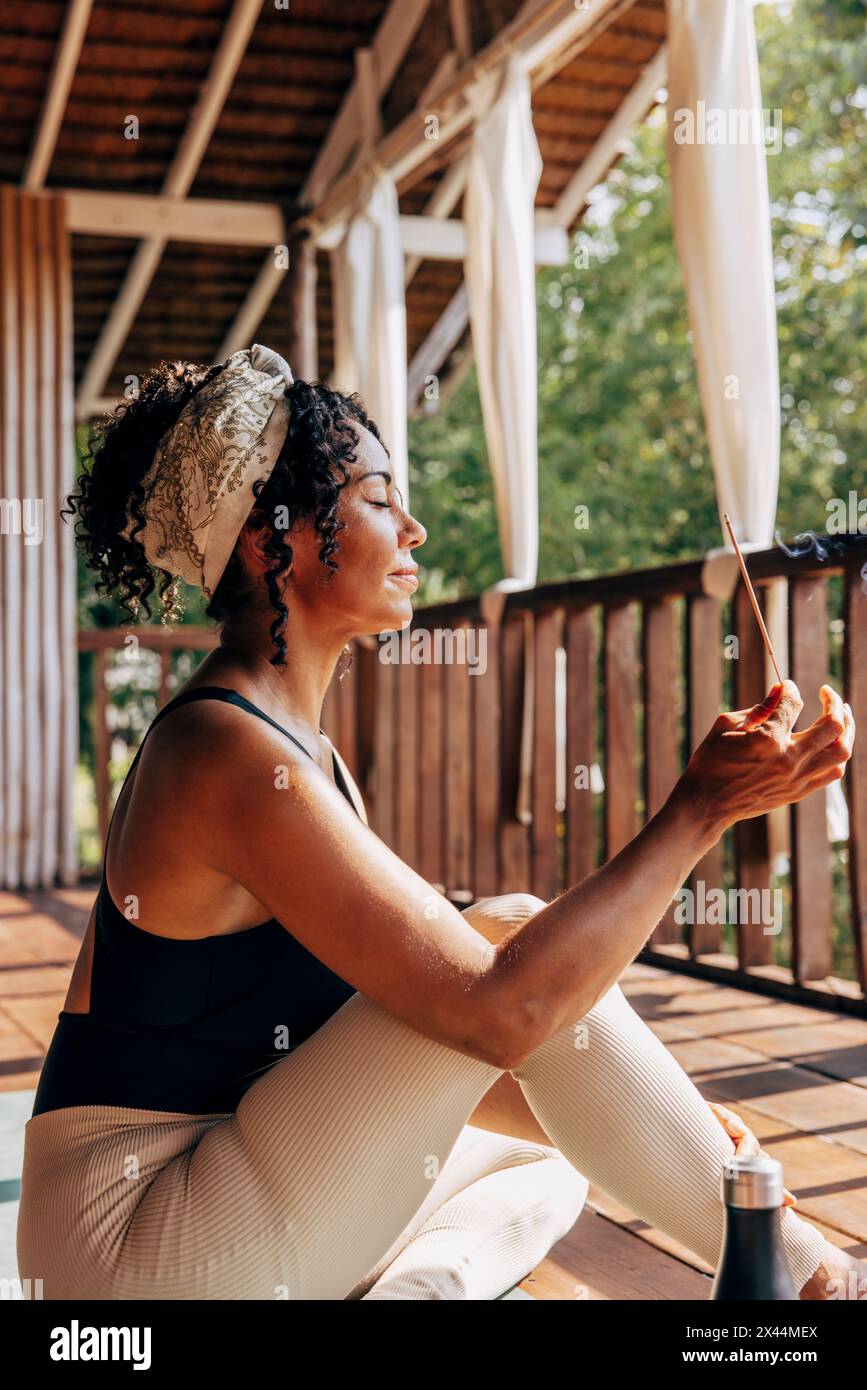 Side view of woman practicing meditation holding incense stick while ...