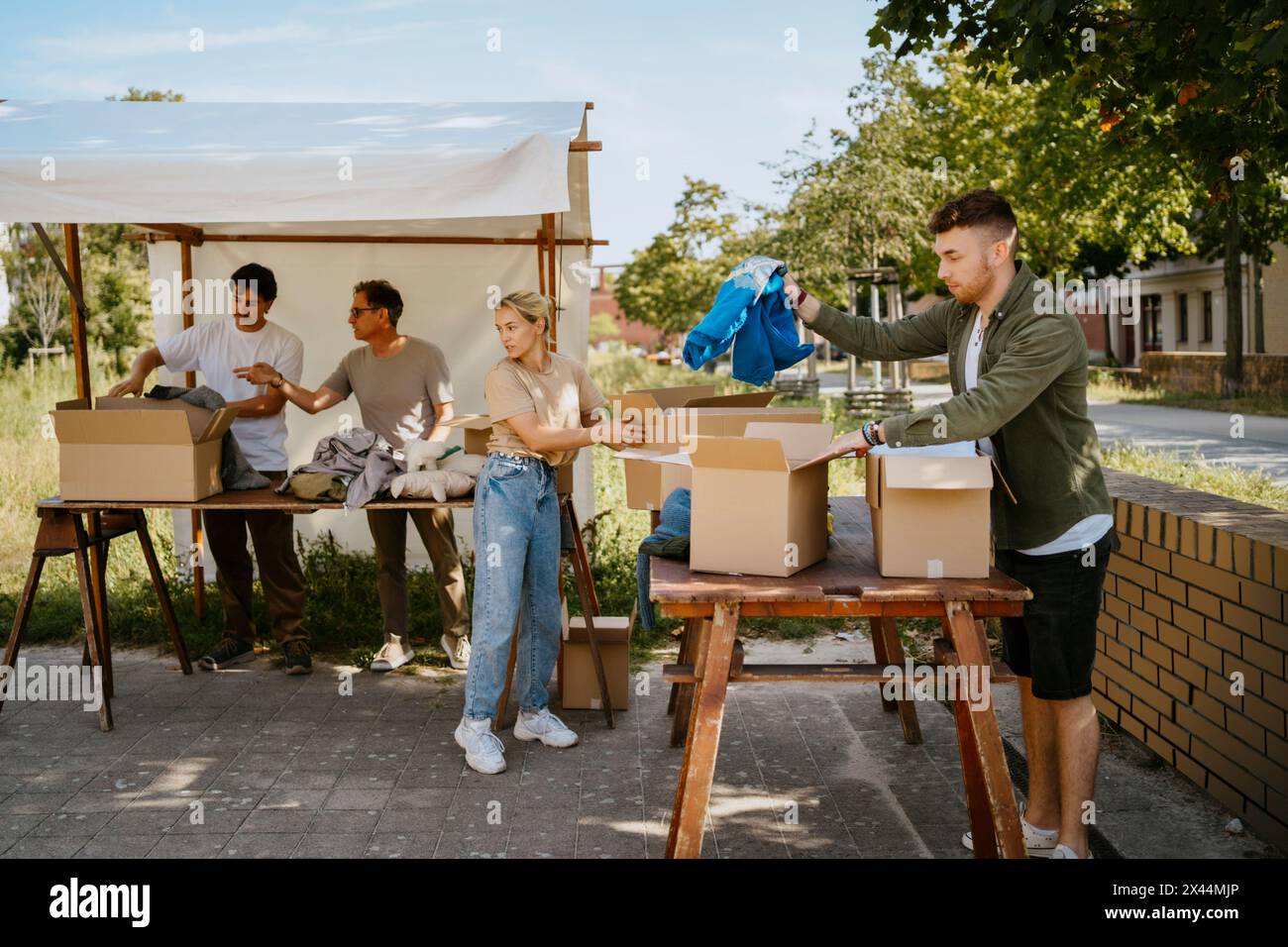 Group of male and female volunteers sorting clothes from cardboard ...