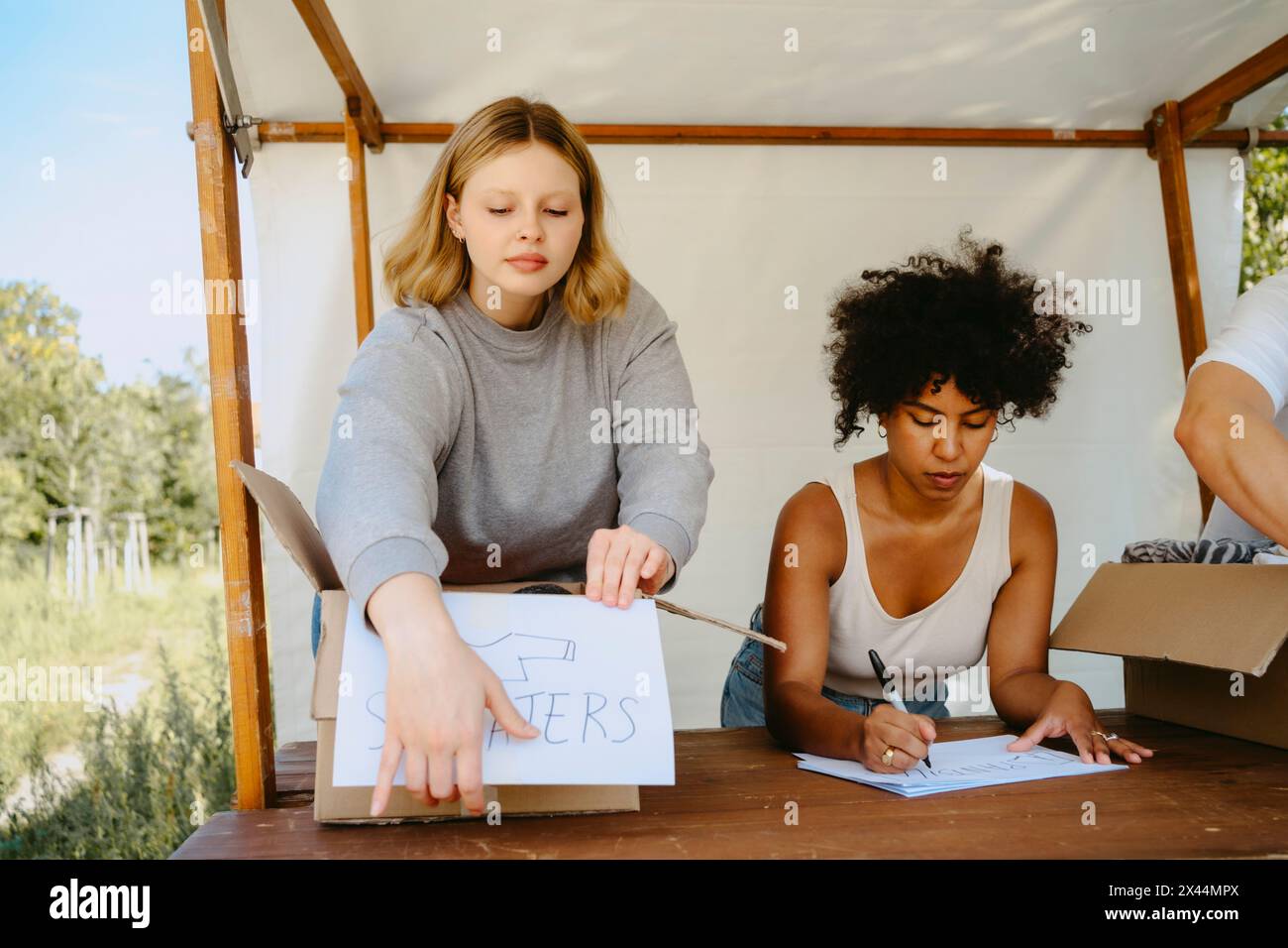 Volunteer helping female colleague while labeling boxes on table during ...