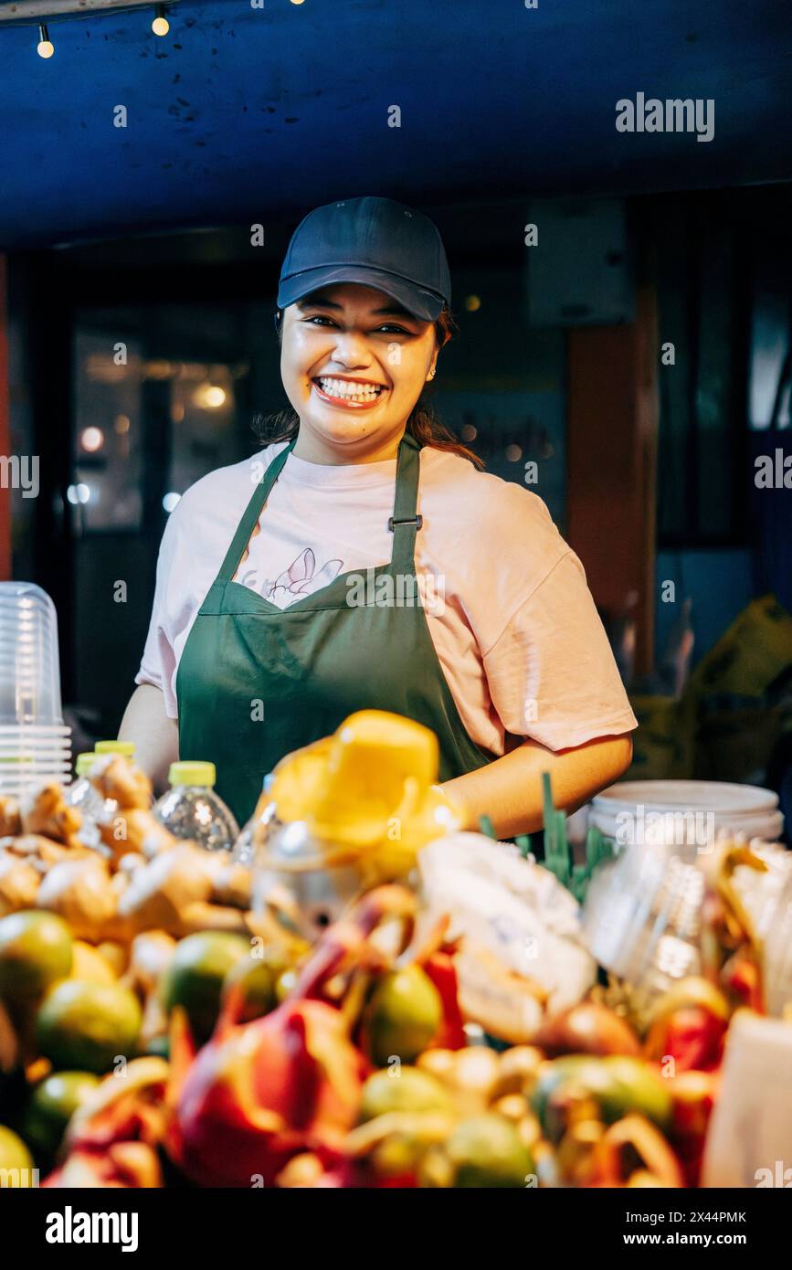 Portrait of smiling female juice vendor standing at stall in food ...