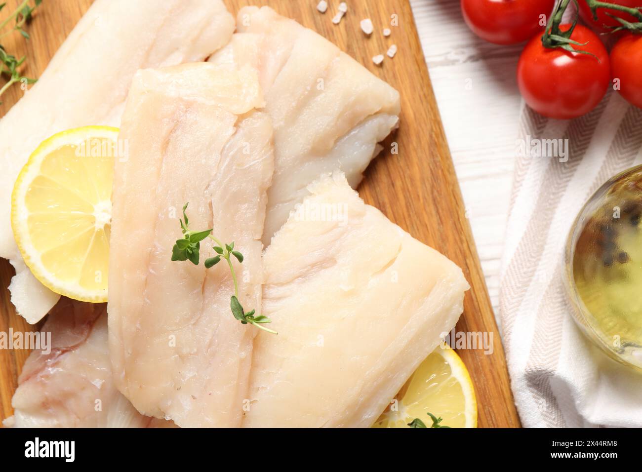 Pieces of raw cod fish, lemon and tomatoes on white wooden table, top ...