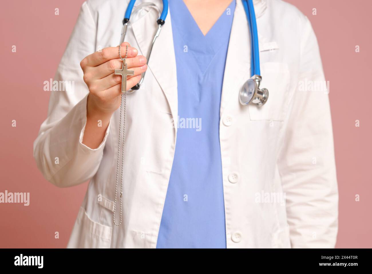 Female doctor holding a Catholic religious cross, studio pink ...
