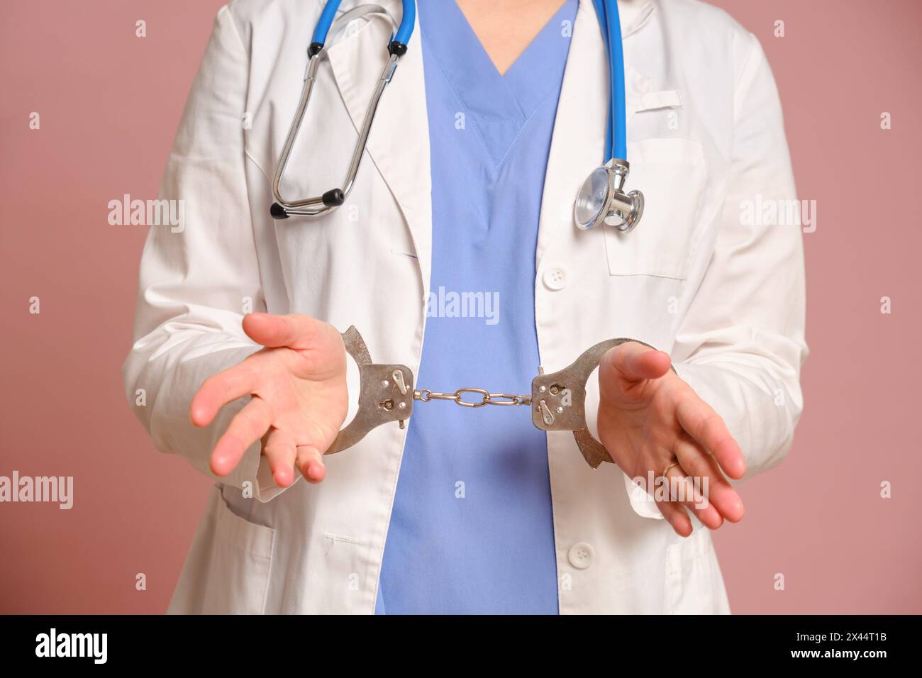 Female doctor with hands handcuffed during arrest, studio pink ...