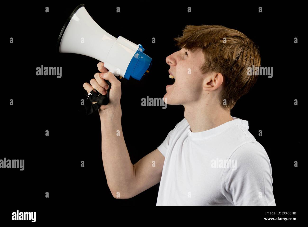 A 15 year old teenage boy shouting into a megaphone against a black ...