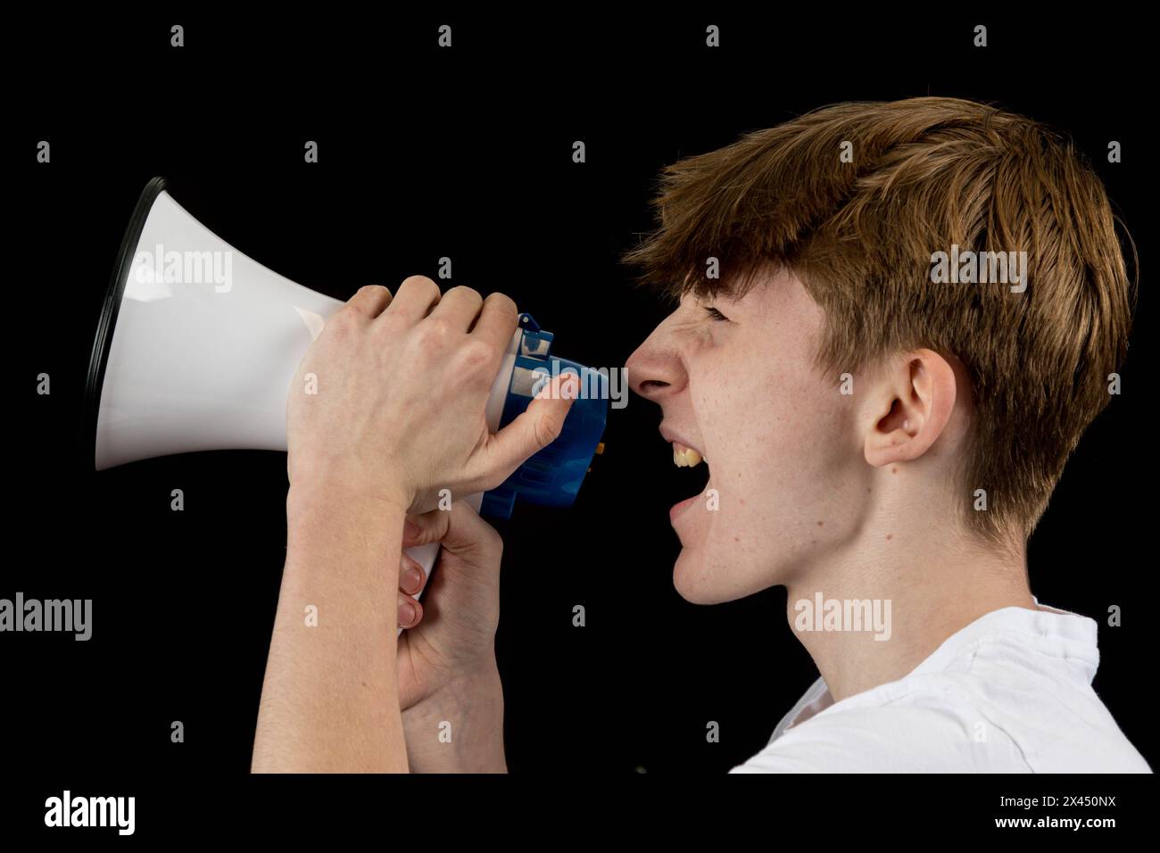 A 15 year old teenage boy shouting into a megaphone against a black ...