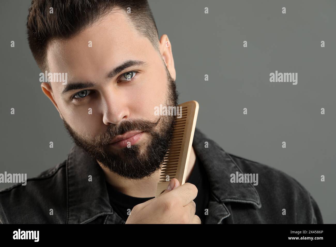 Handsome young man combing beard on grey background Stock Photo - Alamy