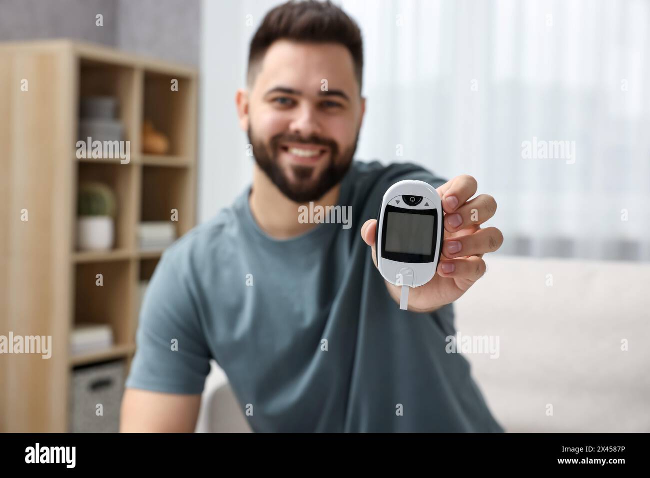 Diabetes test. Smiling man showing glucometer at home, selective focus ...