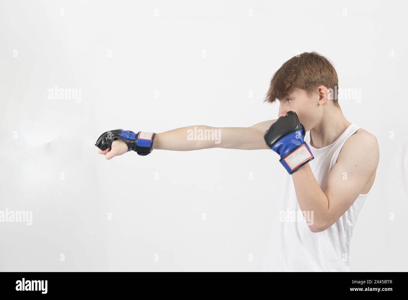 A 15 year old male teenager boxer, wearing a sleeveless top, punching ...