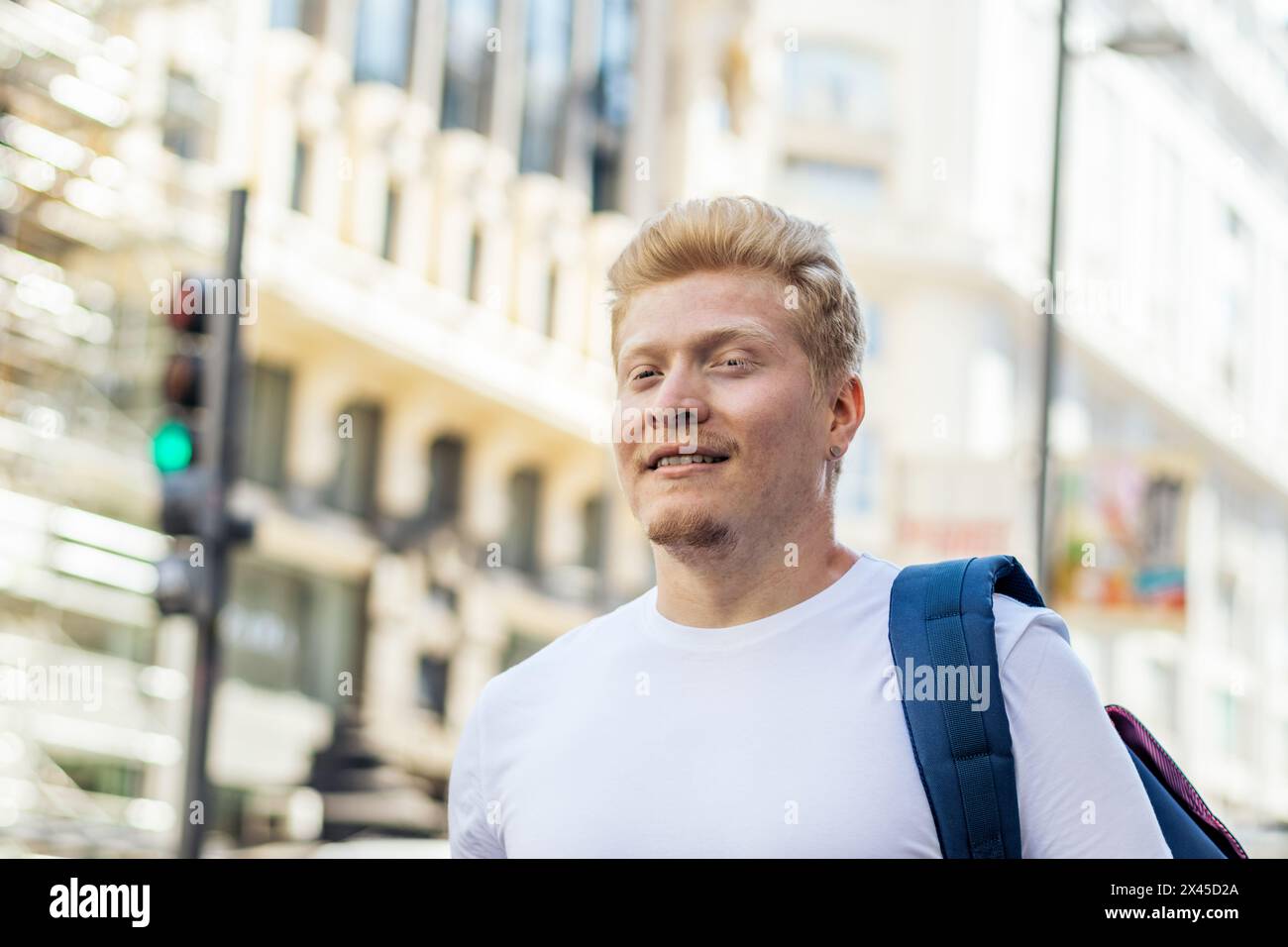Albino latino man dressed in white clothes and backpack walking in the city street . His long ...