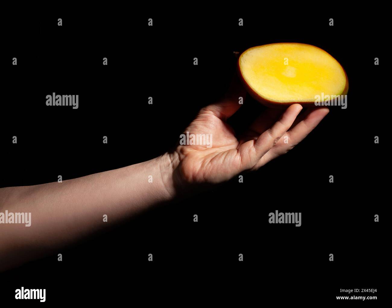 sliced mango in hand on black background Stock Photo - Alamy