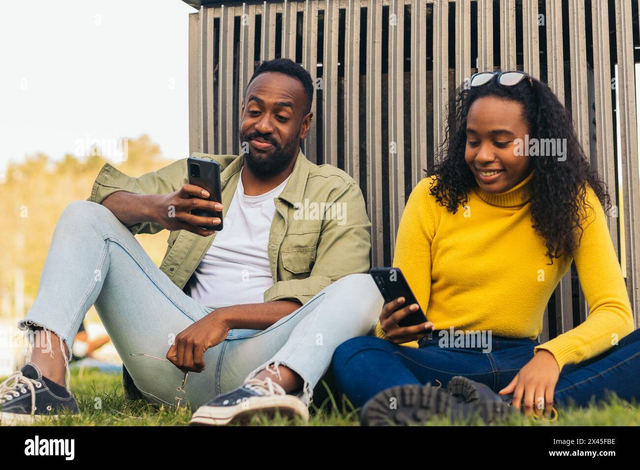 black couple sitting in a park using mobile Stock Photo - Alamy