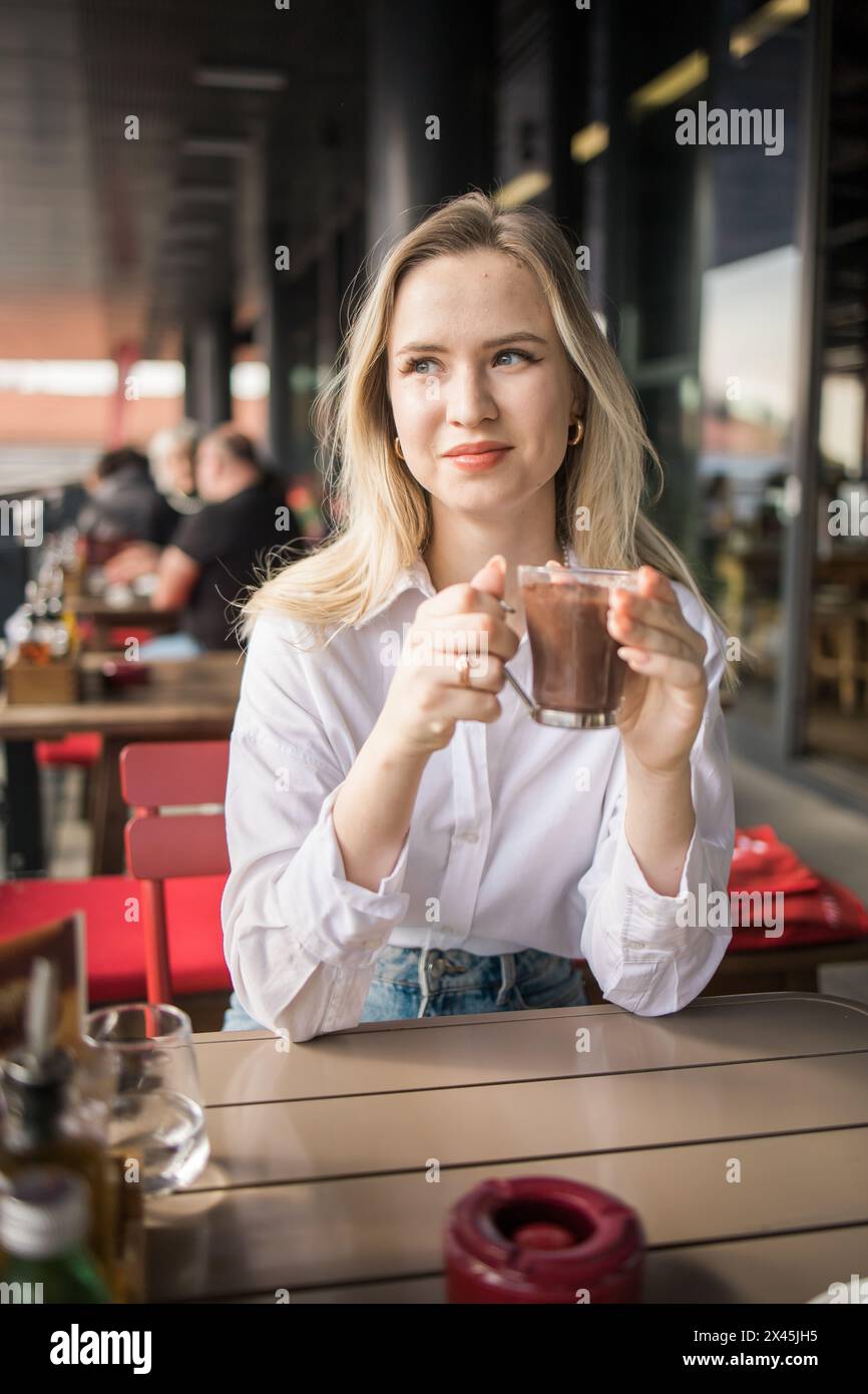 Gen z blonde woman drinks hot chocolate in summer cafe. Tasty beverage ...