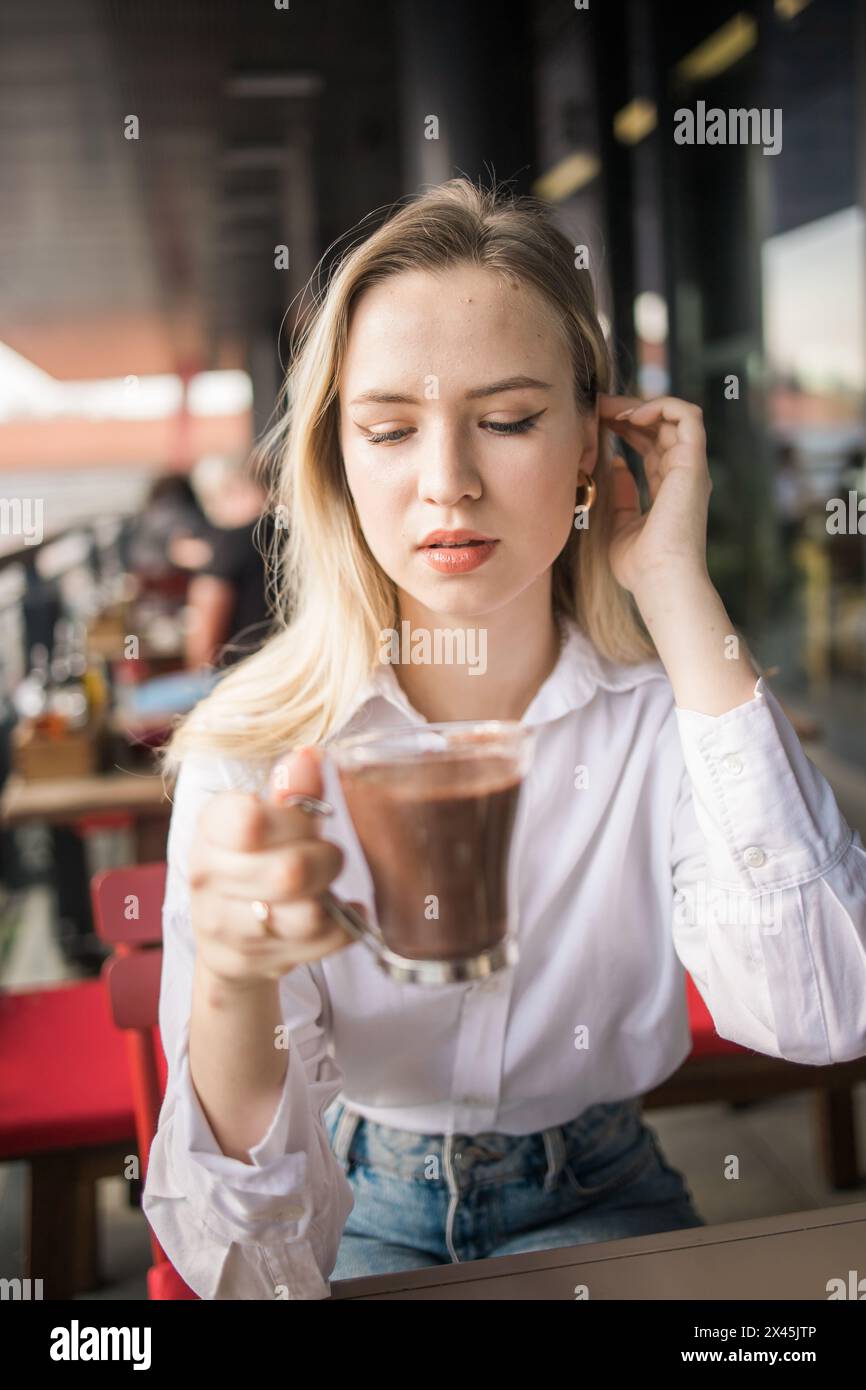 Gen z blonde woman drinks hot chocolate in summer cafe. Tasty beverage ...