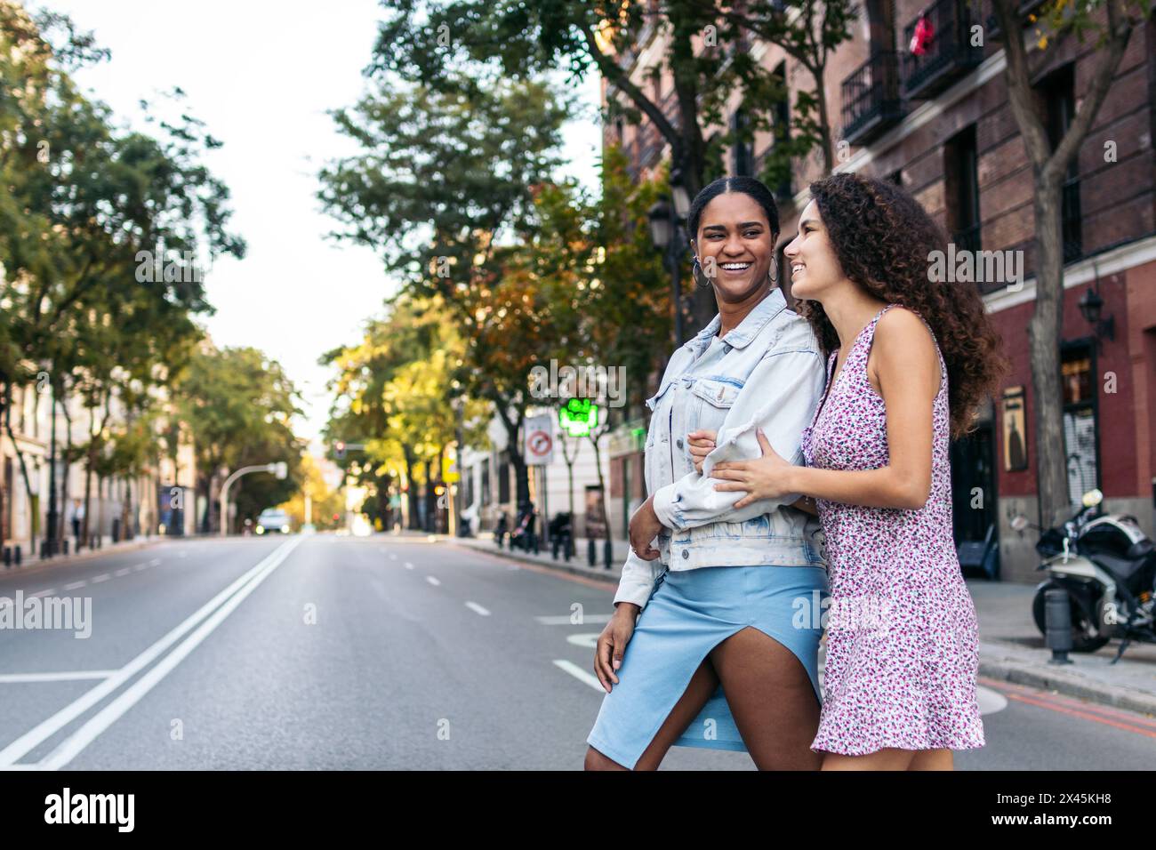 Two young women, friends, crossing the pedestrian crossing in the city ...