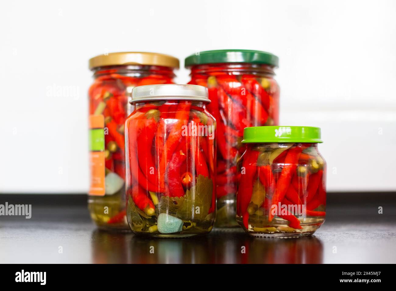 Pickled red hot hot chili peppers in jars on a black table. Canning ...