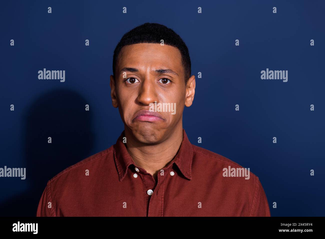 Photo of young man sullen face wear brown shirt isolated on dark blue ...