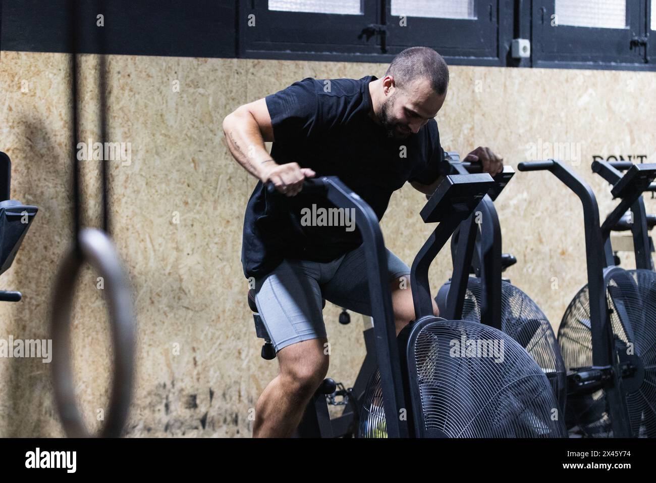 Focused male exercising on air bike during intense functional workout ...