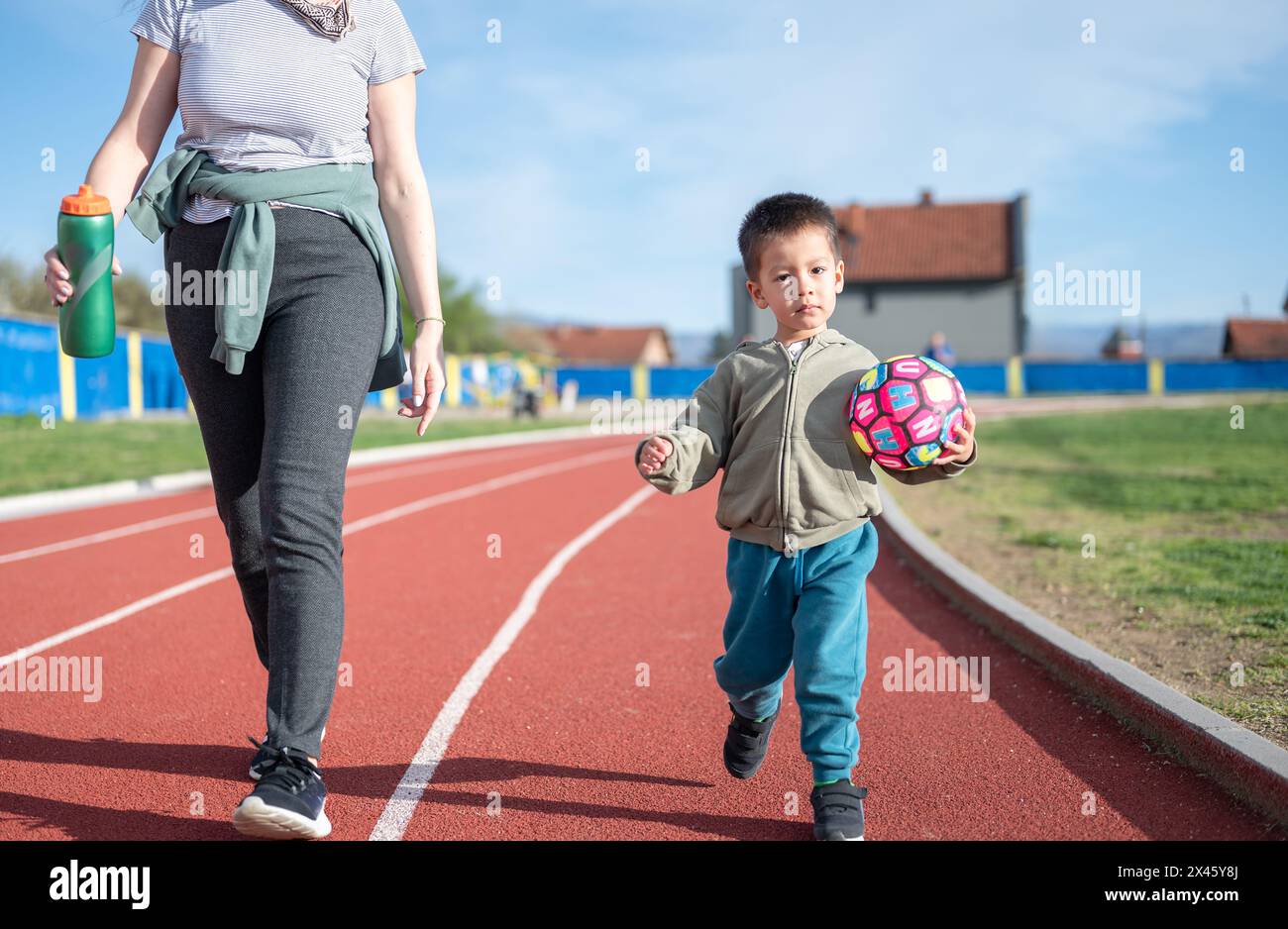 A 3 year old toddler excitedly runs with a soccer ball on a track field ...