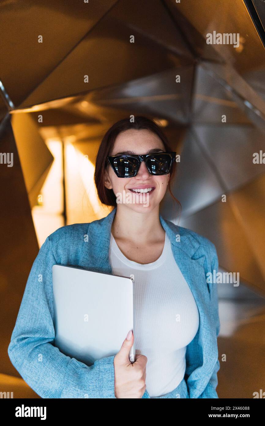 Stylish female in sunglasses with modern netbook in hand walking in ...