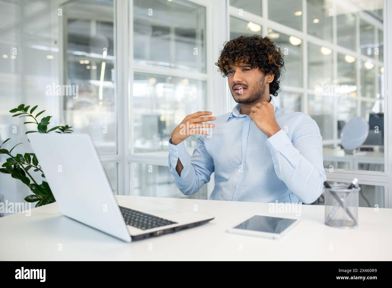 A young businessman loosens his tie, feeling hot and stressed in a ...