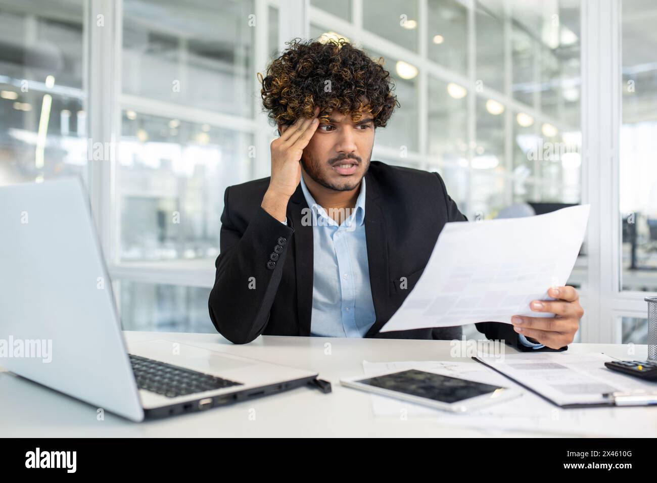 A stressed business professional in suit looks over important documents ...