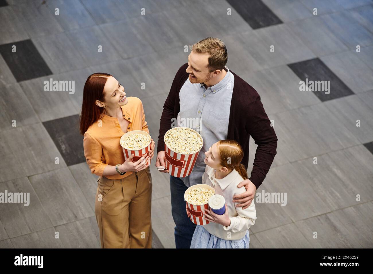 A man and woman excitedly hold popcorn buckets while a child smiles ...