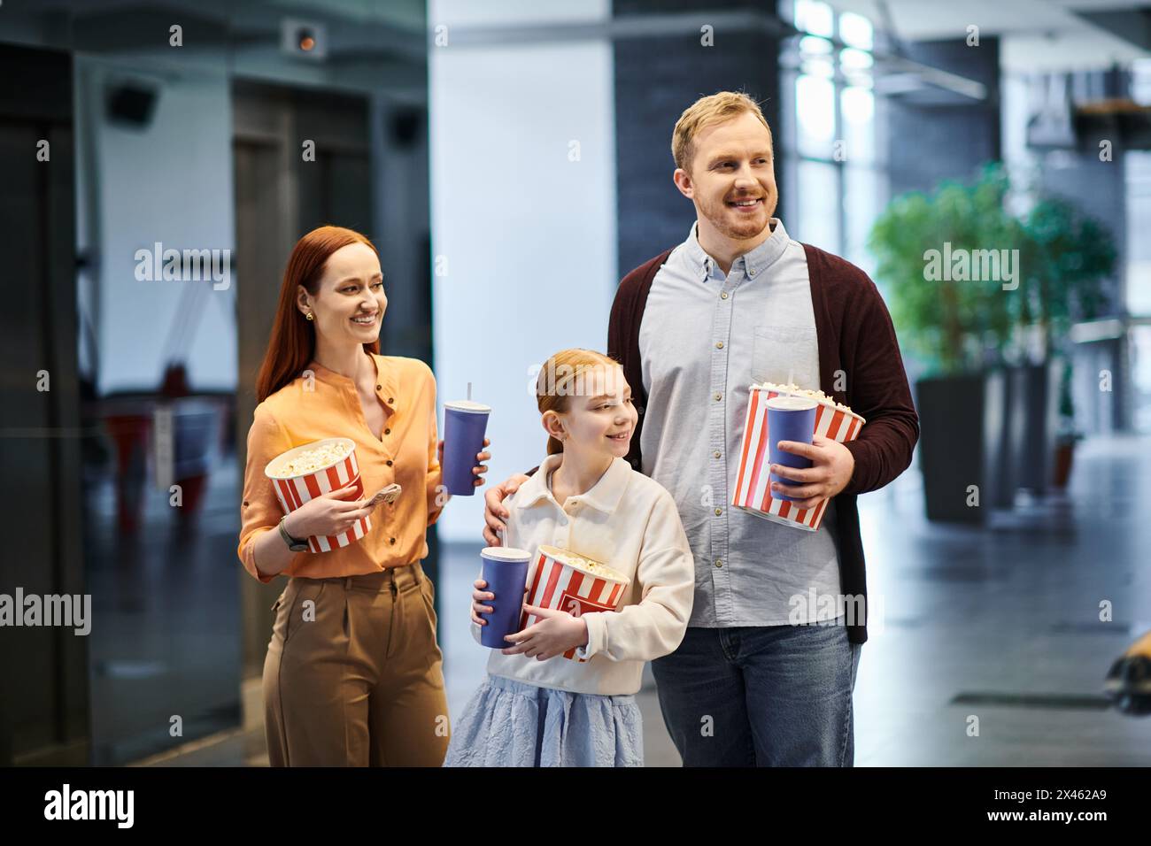 A man, woman, and child happily hold popcorn in their hands while ...