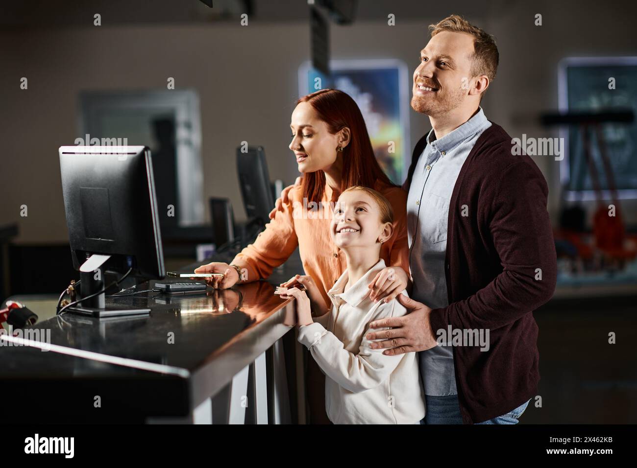 A couple standing in front of a computer with their kid, engrossed in ...